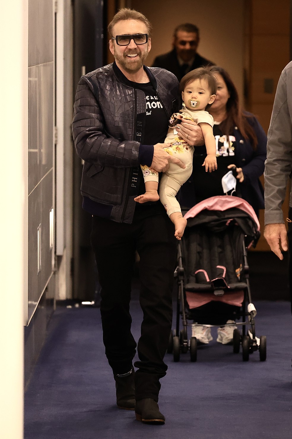 Nicolas Cage chega sorridente na Austrália com a filha caçula nos braços