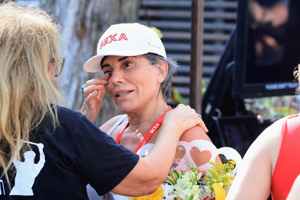 Gloria Pires recebe flores e se emociona com fãs durante gravação na praia