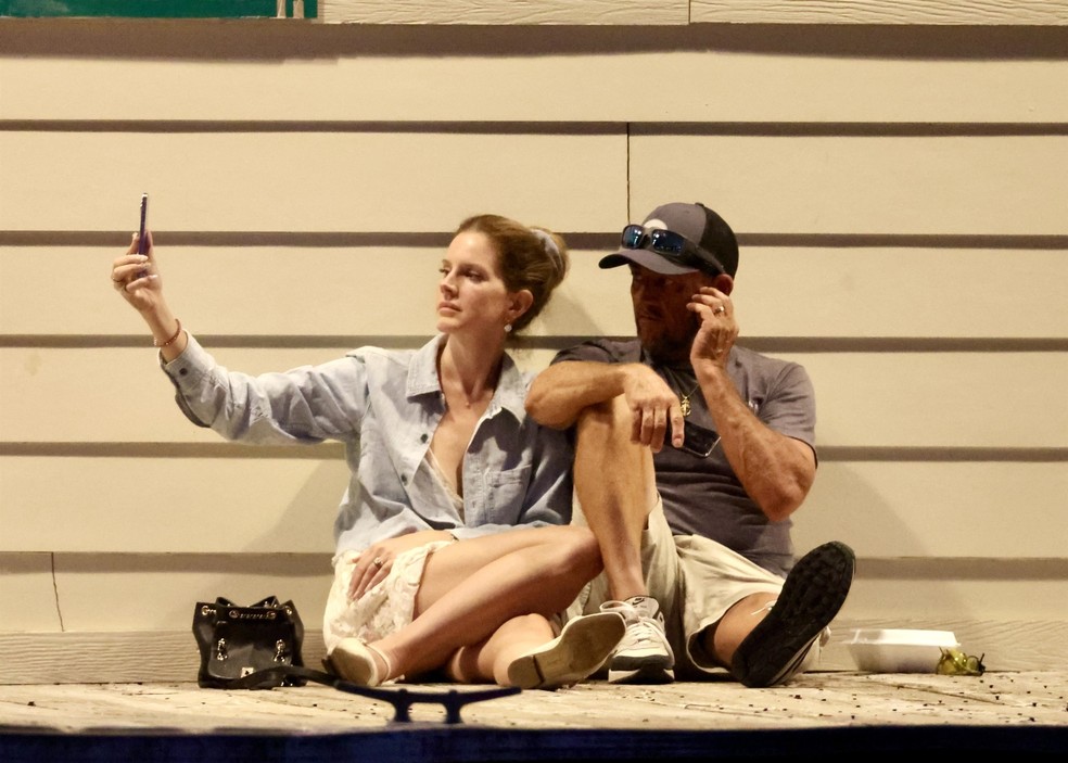 Recém-casados, Lana Del Rey e o marido relaxam no chão após jantar e levam marmita